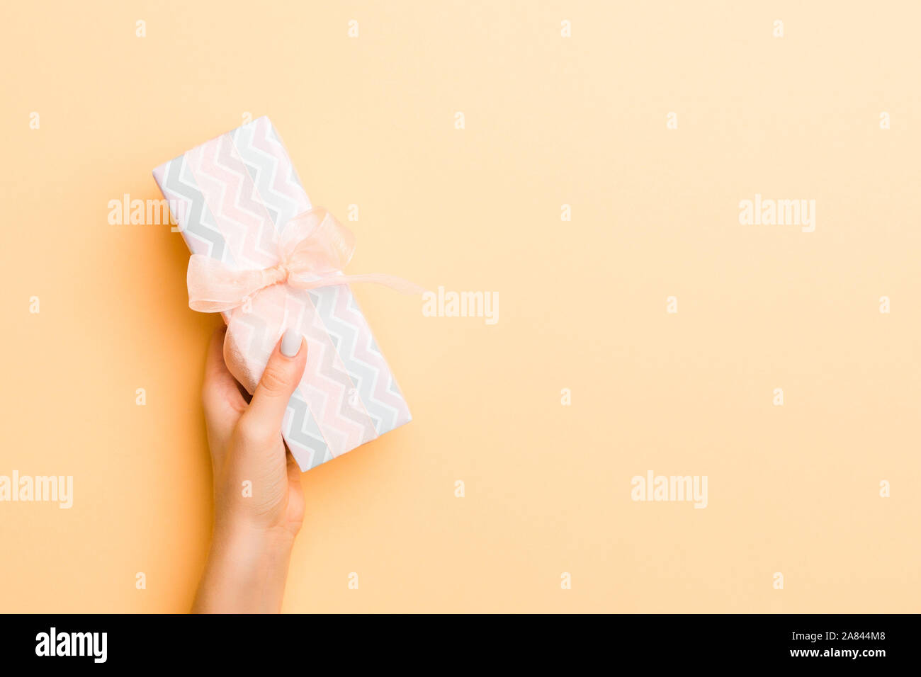Flat lay of woman hands holding gift wrapped and decorated with bow on ...