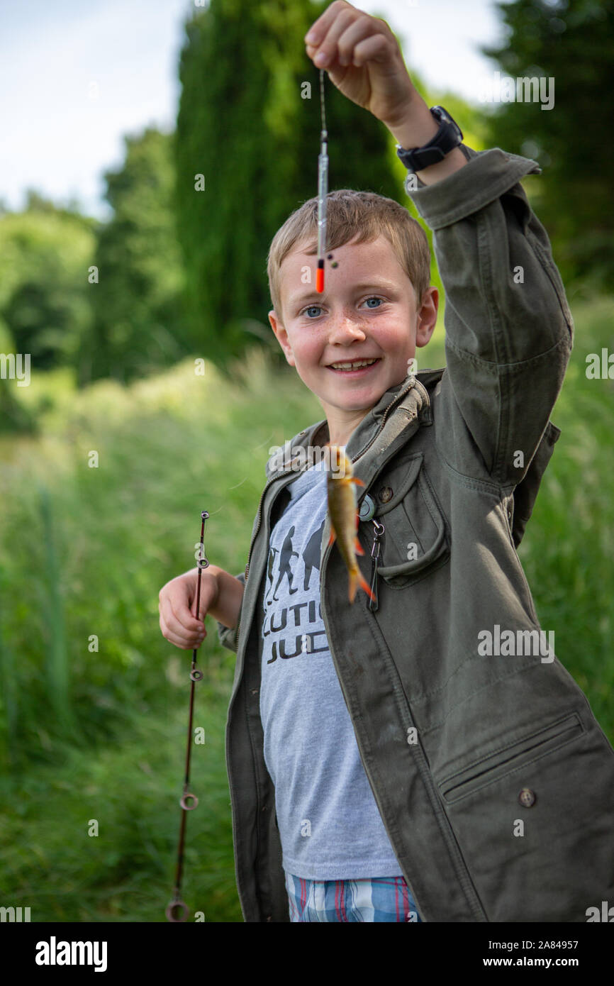 A young boy smiling at the camera as he hold us a fish he has caught ...