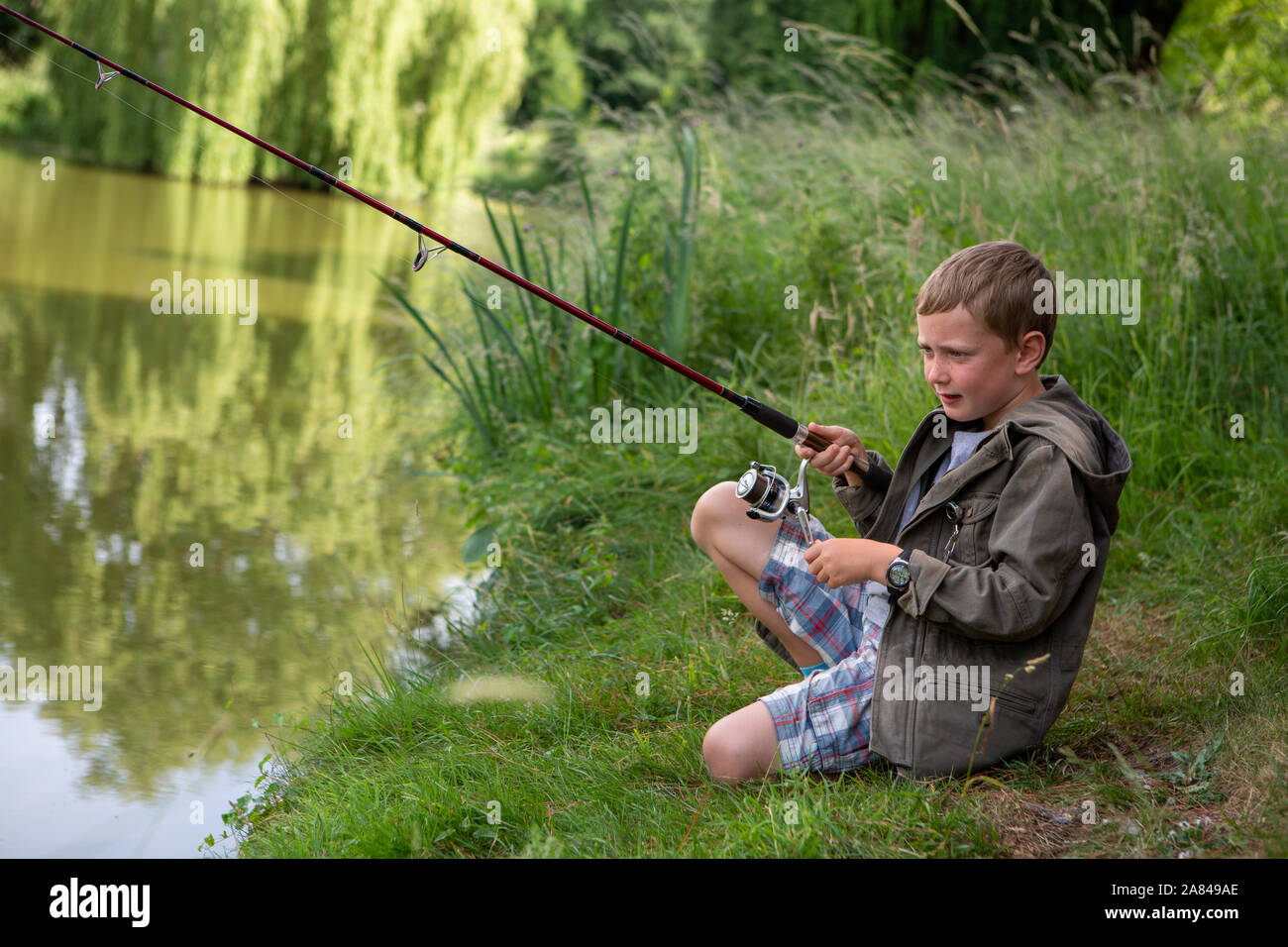 A young boy holding his fishing rod next to a lake Stock Photo - Alamy