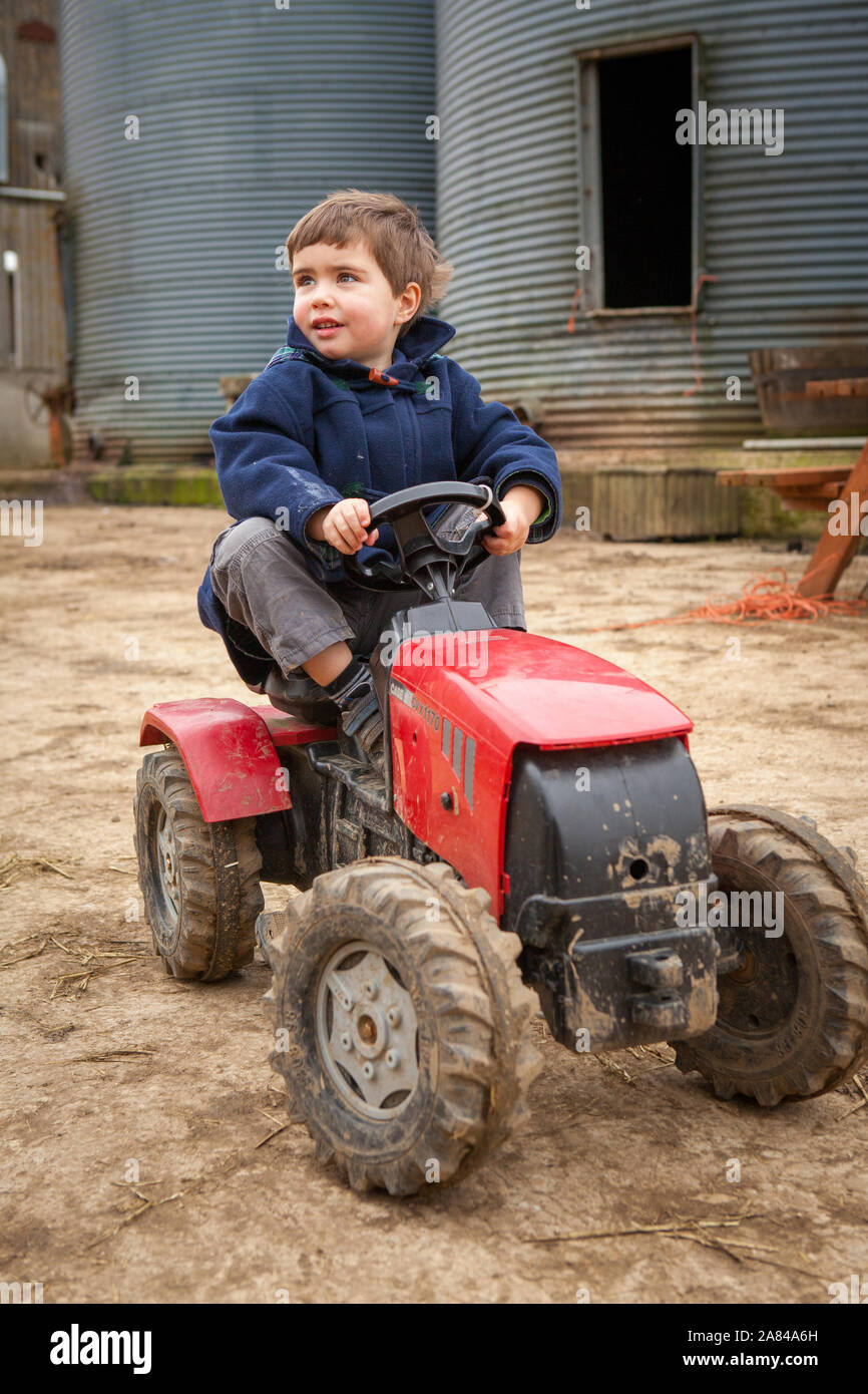 A young boy driving a toy tractor in a farmyard, England Stock Photo ...