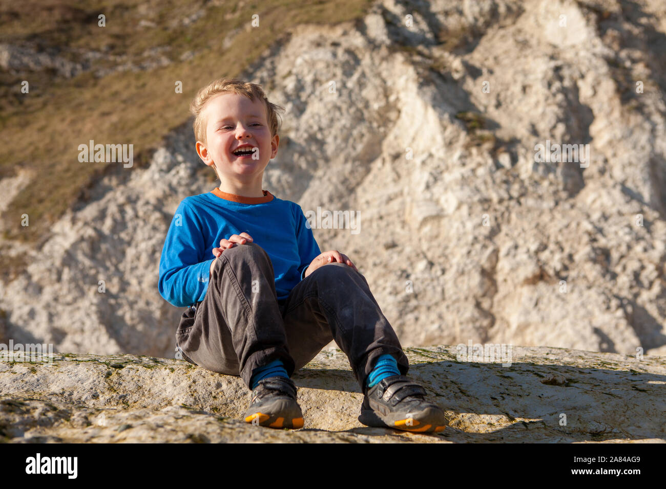 A young boy sitting laughing on the rocks at the beach Stock Photo - Alamy