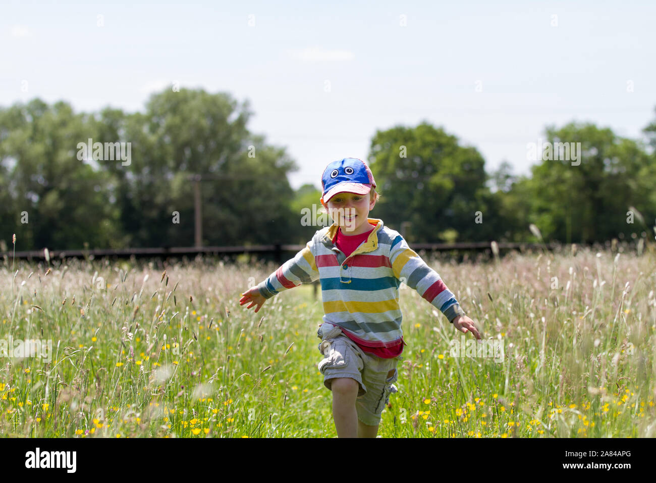 A boy running through a field of wild flowers with his hands stretched ...