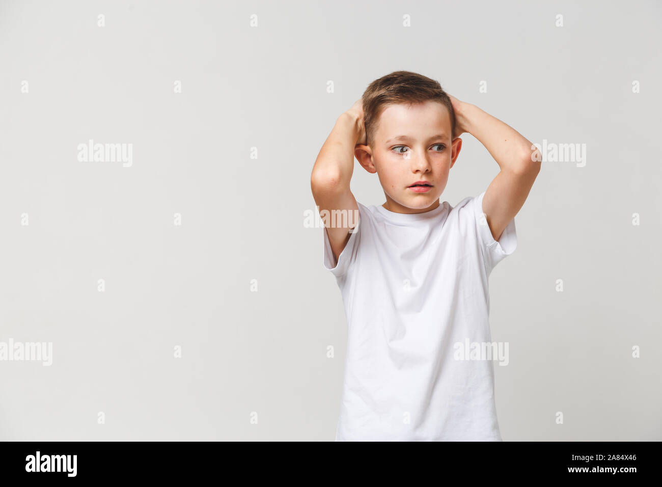 Terrified boy in white t-shirt with both hands on head on gray ...