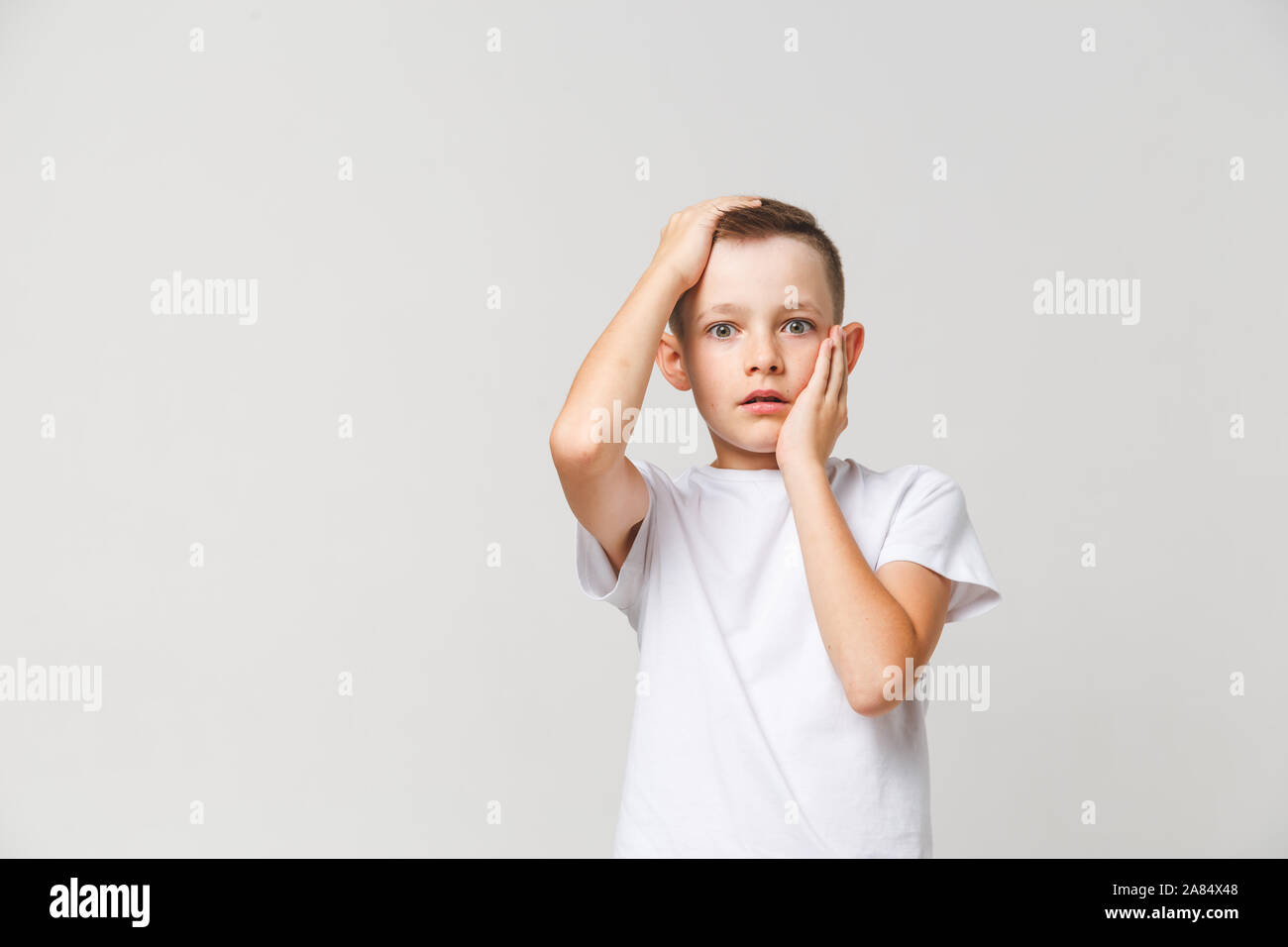 Terrified boy in white t-shirt with both hands on head on gray ...