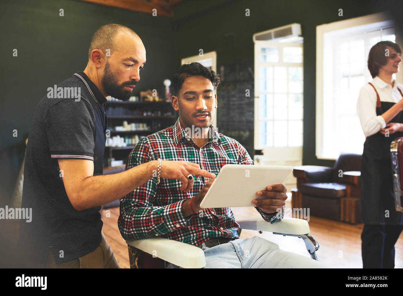 Male barber and customer with digital tablet talking in barbershop ...