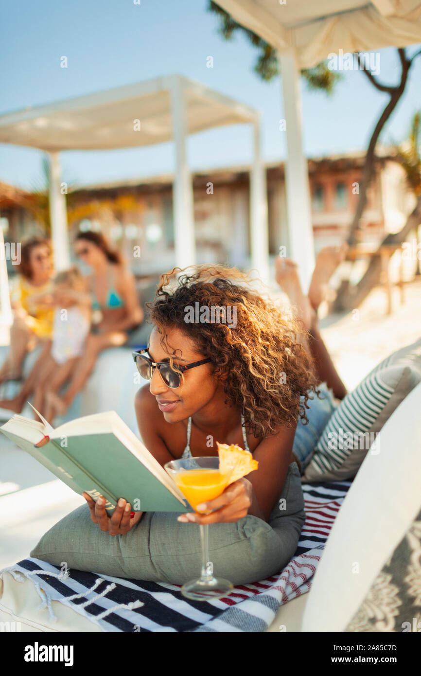 Carefree woman relaxing, reading book and drinking cocktail on beach ...