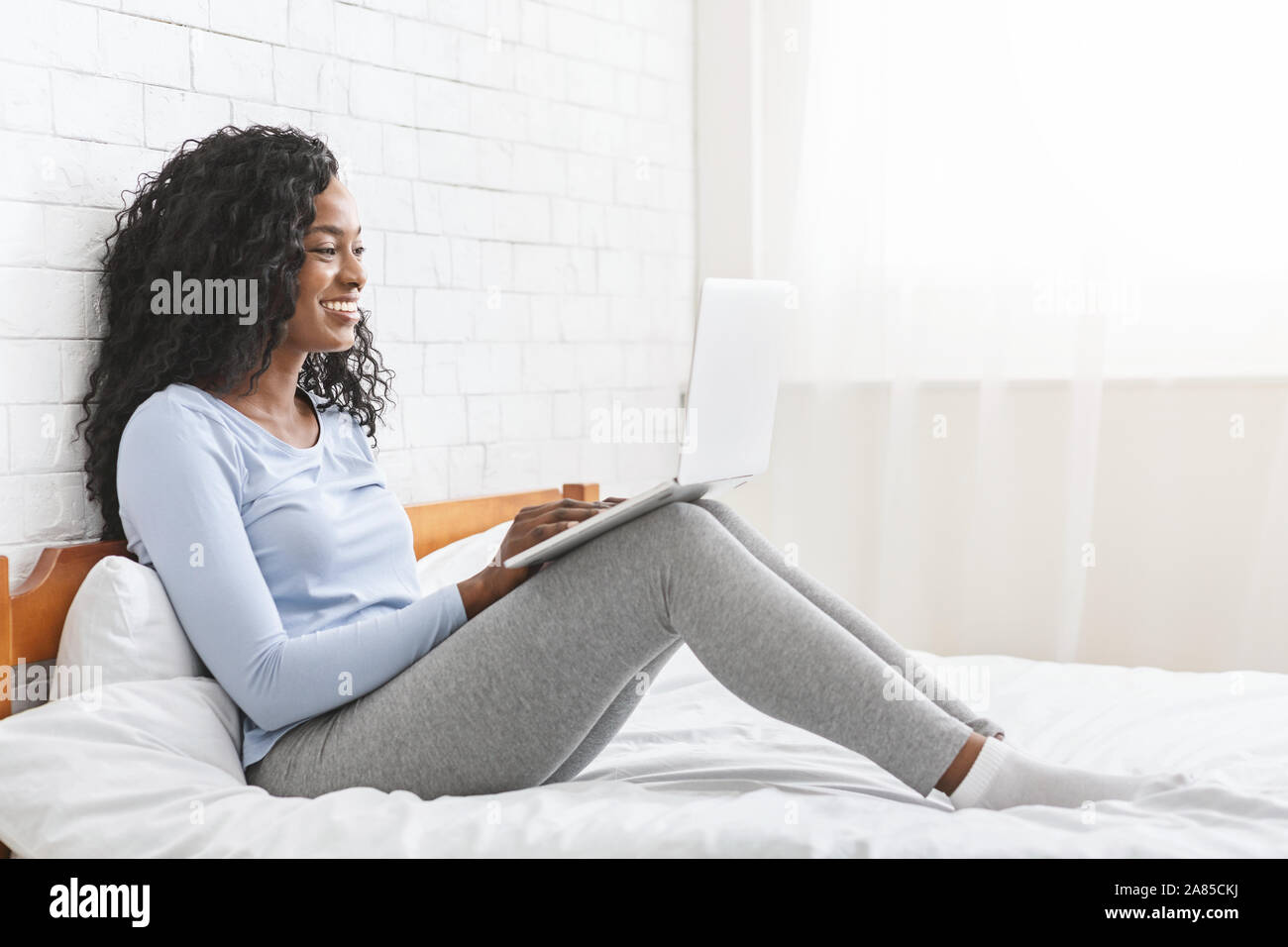 Pretty happy girl sitting on bed, using laptop Stock Photo - Alamy