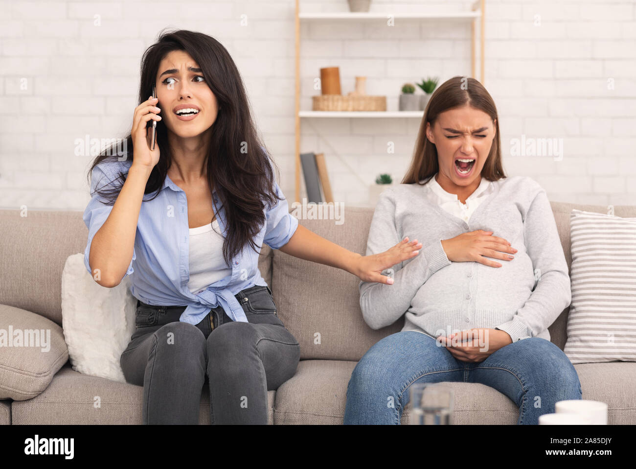 Girl Calling Doctor For Pregnant Friend Having Spasm Sitting Indoor