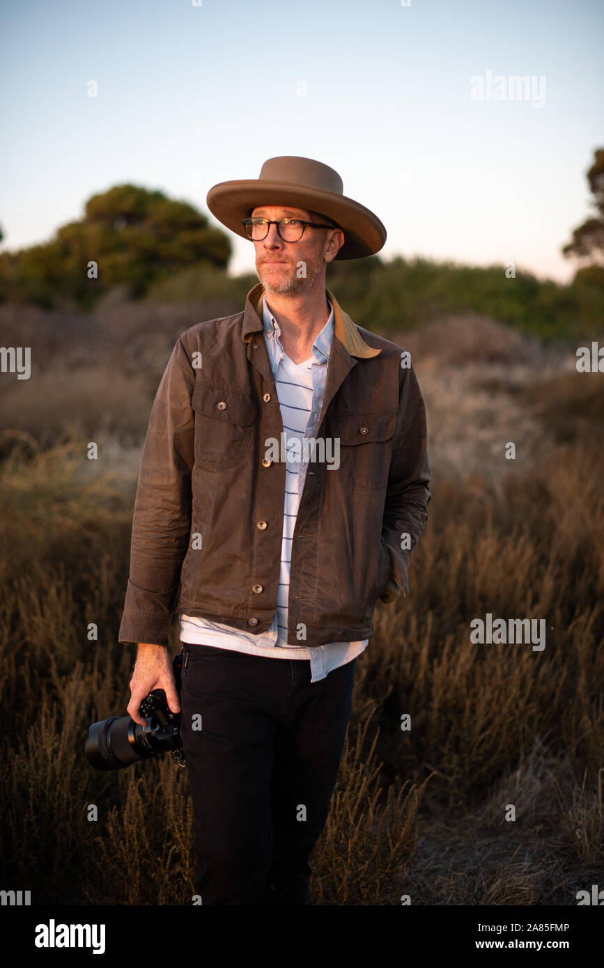 Man standing holding camera looking toward sunset Stock Photo - Alamy
