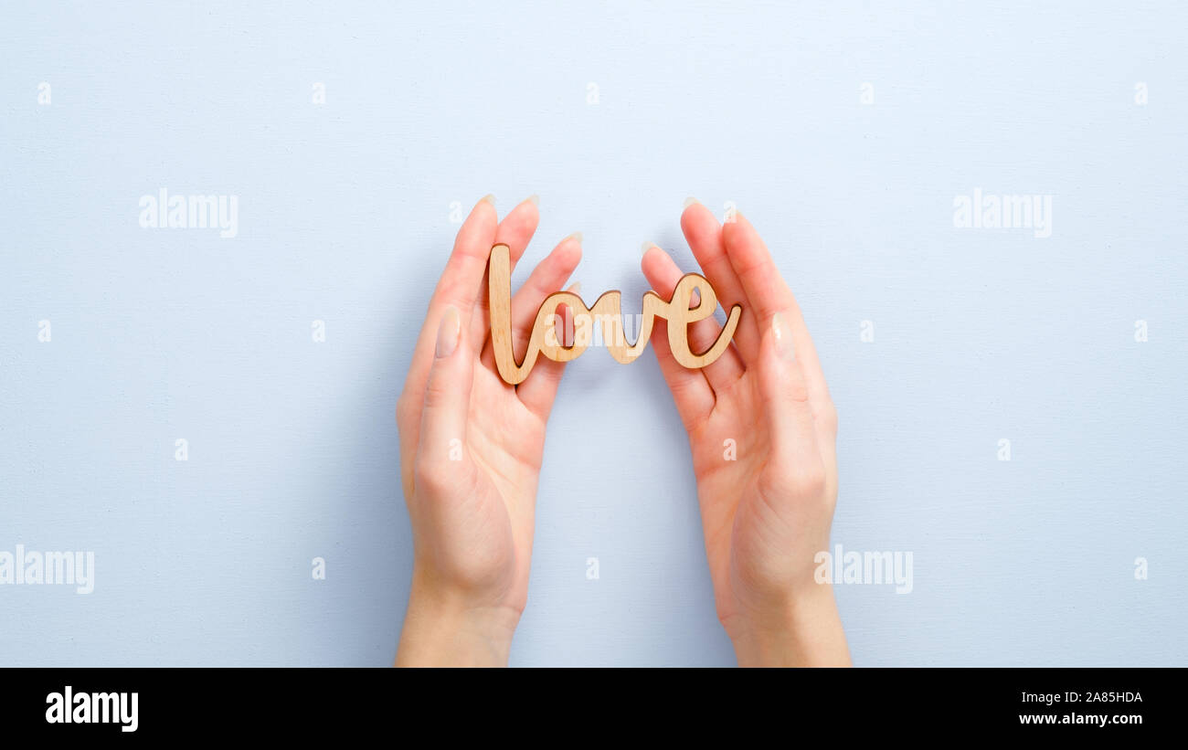 Female hand holding wooden word sign "Love" on blue background. Flat ...