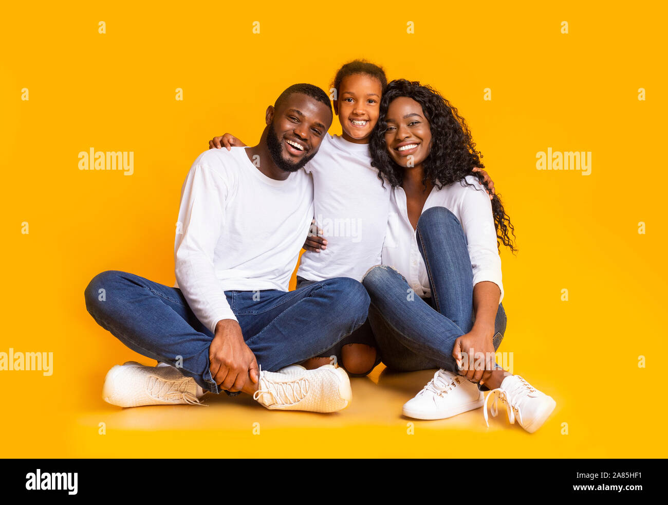 Afro millennial family of three sitting on floor and hugging Stock ...