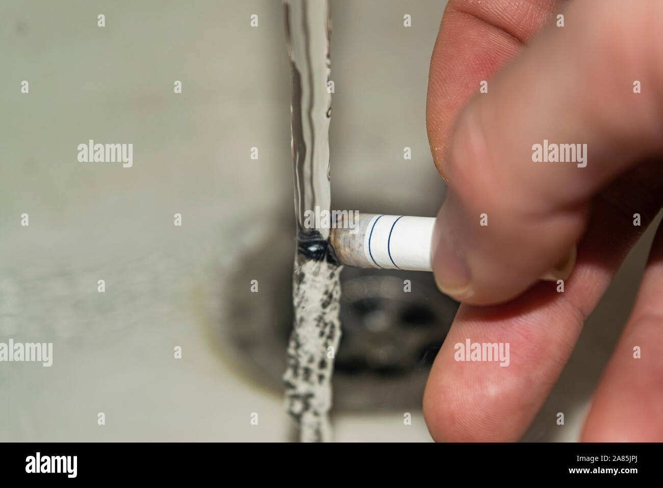 Cigarette in a man's hand extinguished under a stream of water concept ...