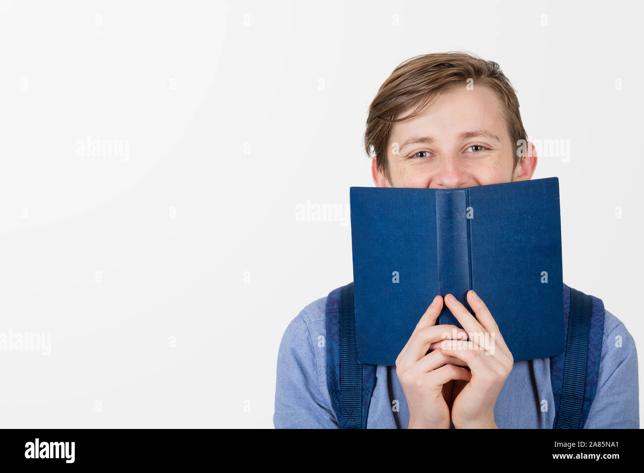 Happy teenager boy smiling covering half face with a opened blue book ...