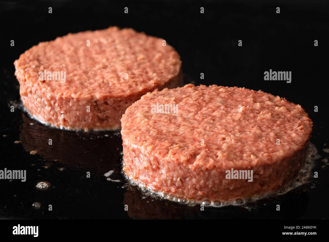 Two uncooked plant based vegetarian burger patties being cooked on flat ...