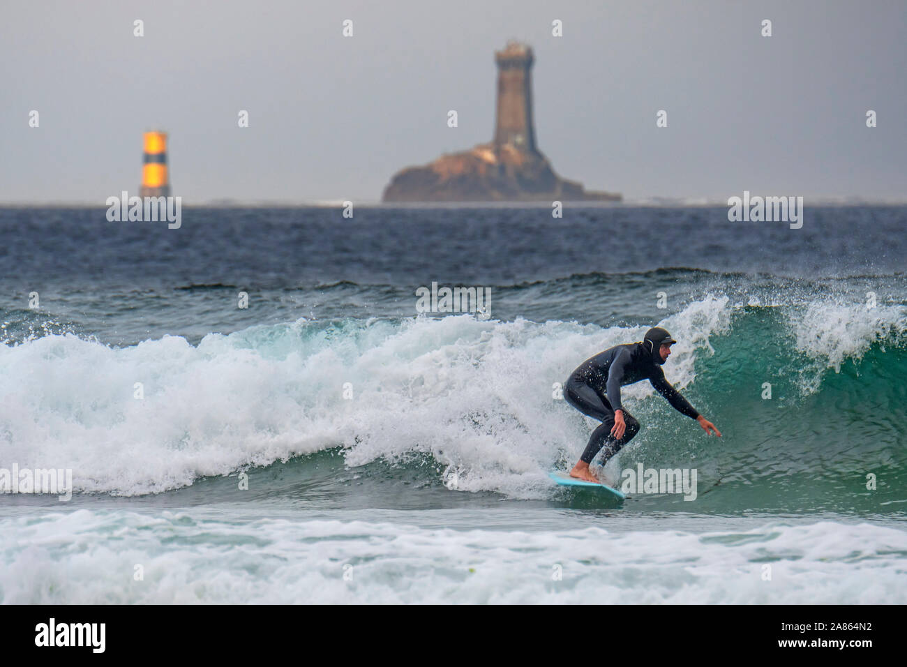 Lighthouse La Vieille and surfer in wetsuit riding a wave on surfboard ...