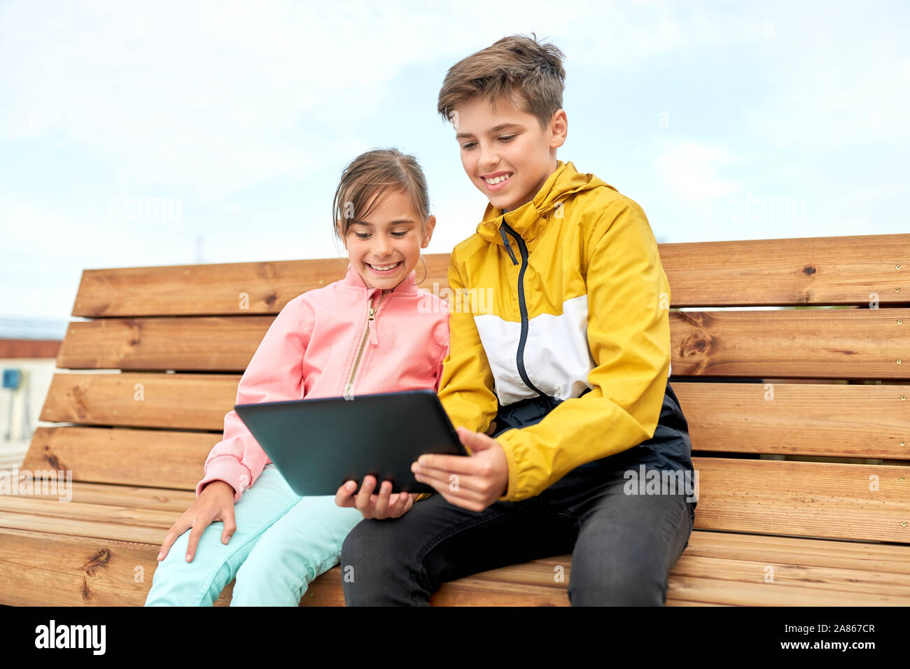 children with tablet computer sitting on bench Stock Photo - Alamy