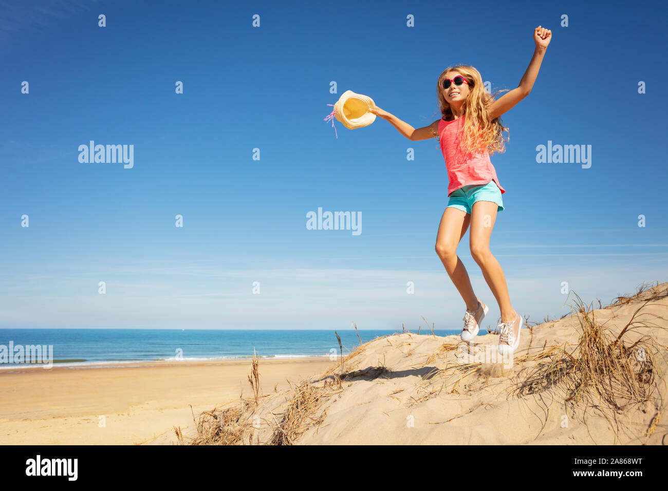 Happy girl with straw hat jump on sand near sea Stock Photo - Alamy