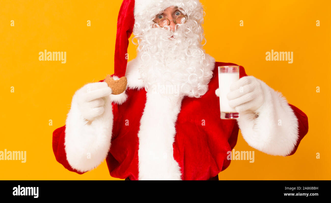 Santa eating cookie and drinking milk on orange background Stock Photo ...