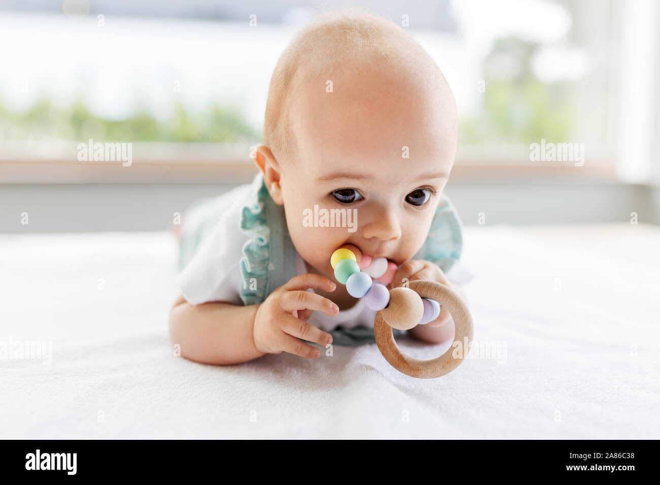baby girl on white blanket chewing wooden rattle Stock Photo - Alamy