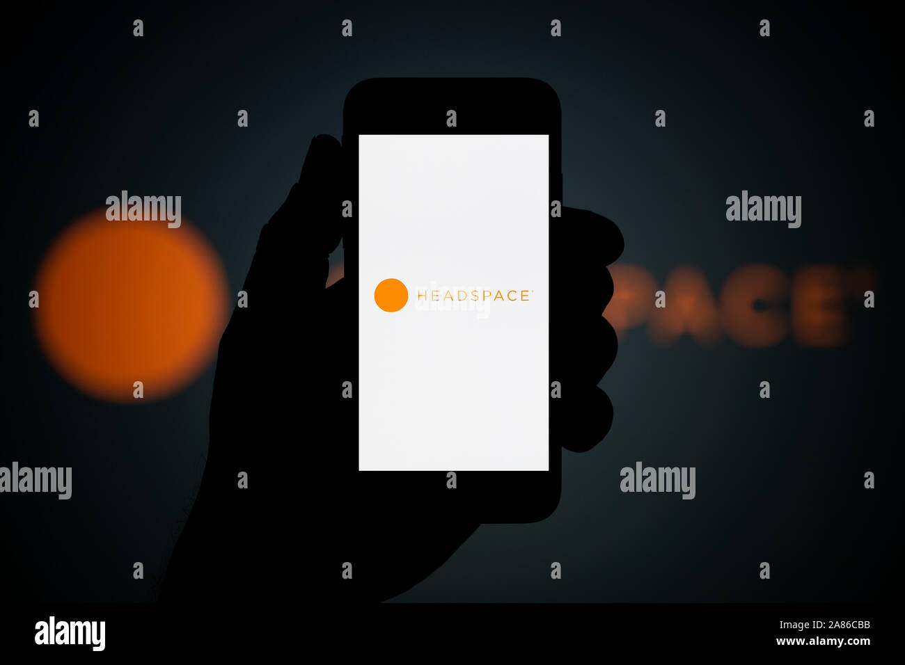 A man looks at his iPhone which displays the Headspace logo, with the ...