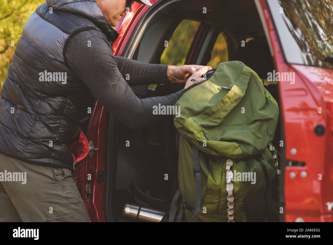 Elderly man tourist prepare for car travel. Touristic equipment at open ...