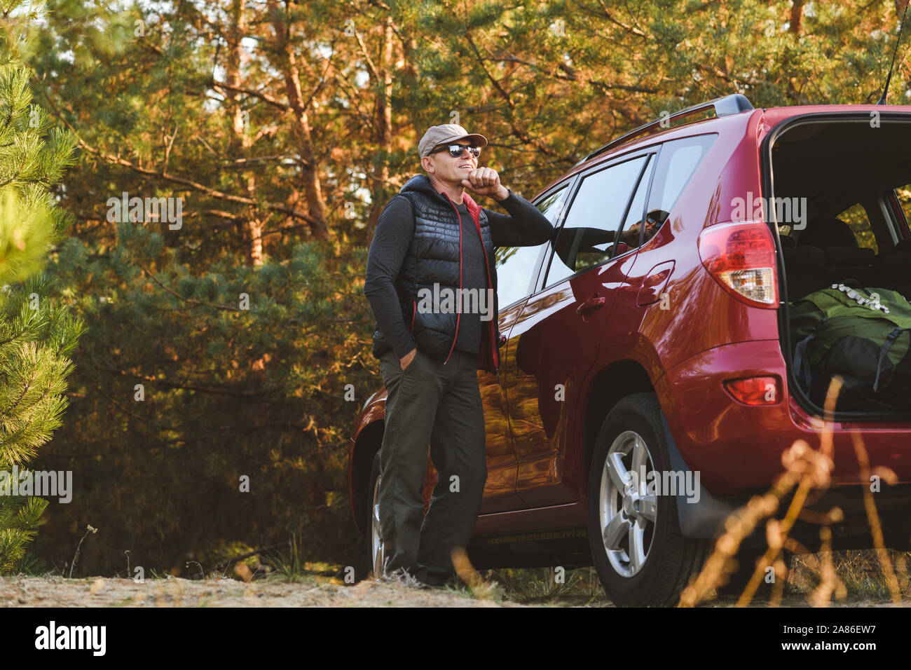 Man lean on car at nature background. An elderly man in tourist clothes ...