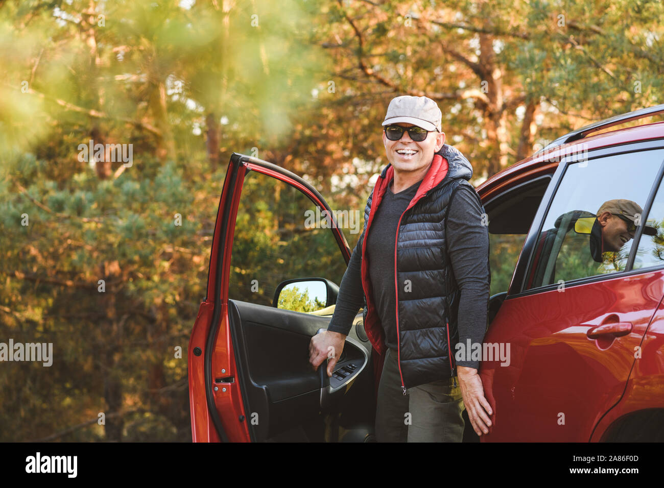 Happy senior man getting out of car, opening door and smiling to camera ...