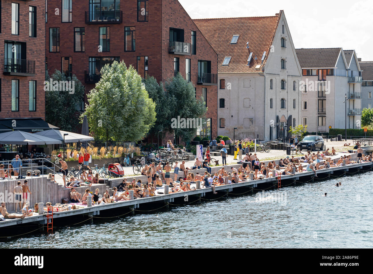 People sitting by Copenhagen Harbour, some swimming in the harbour ...
