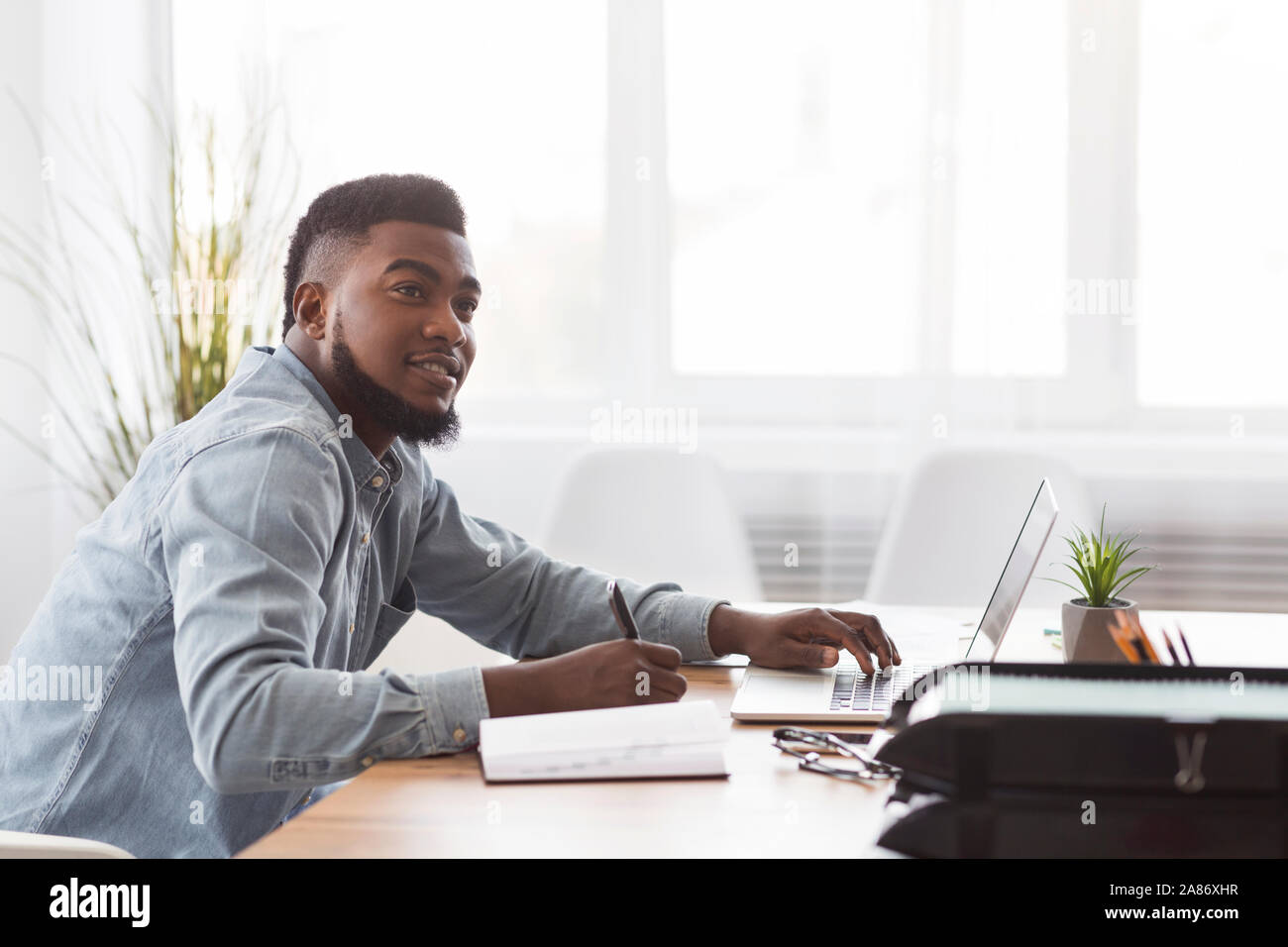 Black man taking notes from laptop at workplace in office Stock Photo ...