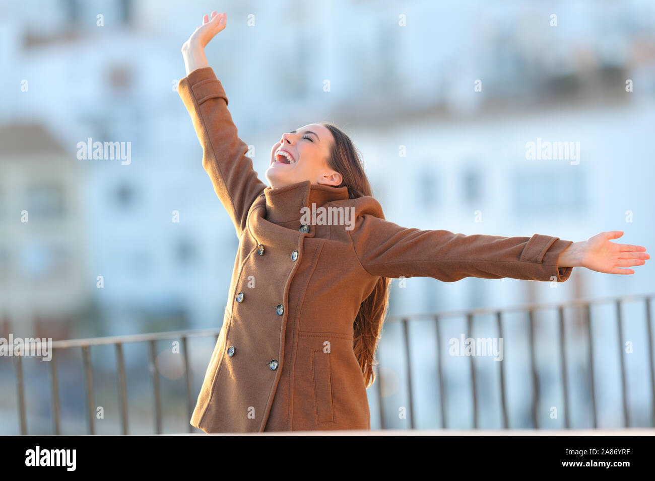 Excited woman wearing jacket raising arms in winter in a balcony Stock ...