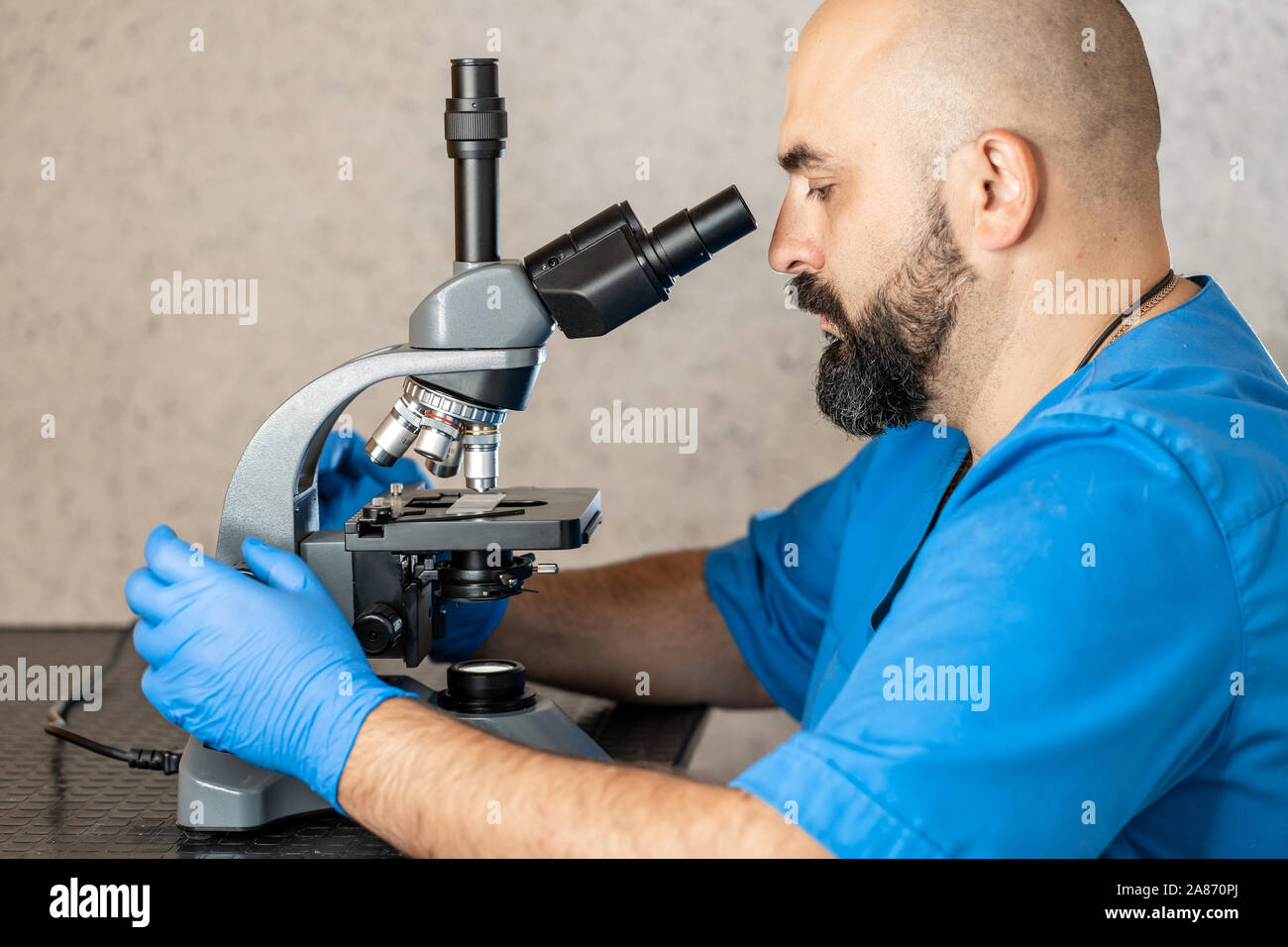 Male laboratory assistant examining biomaterial samples in a microscope ...