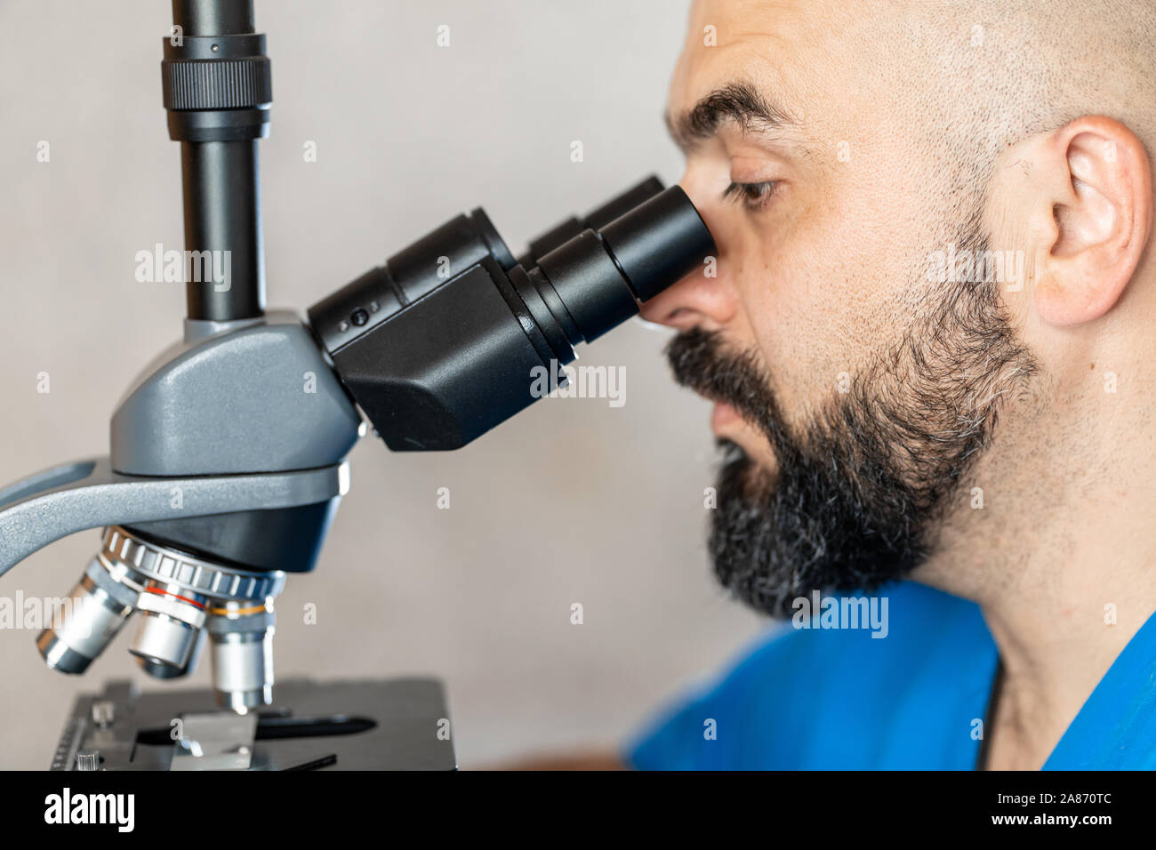 Male laboratory assistant examining biomaterial samples in a microscope ...