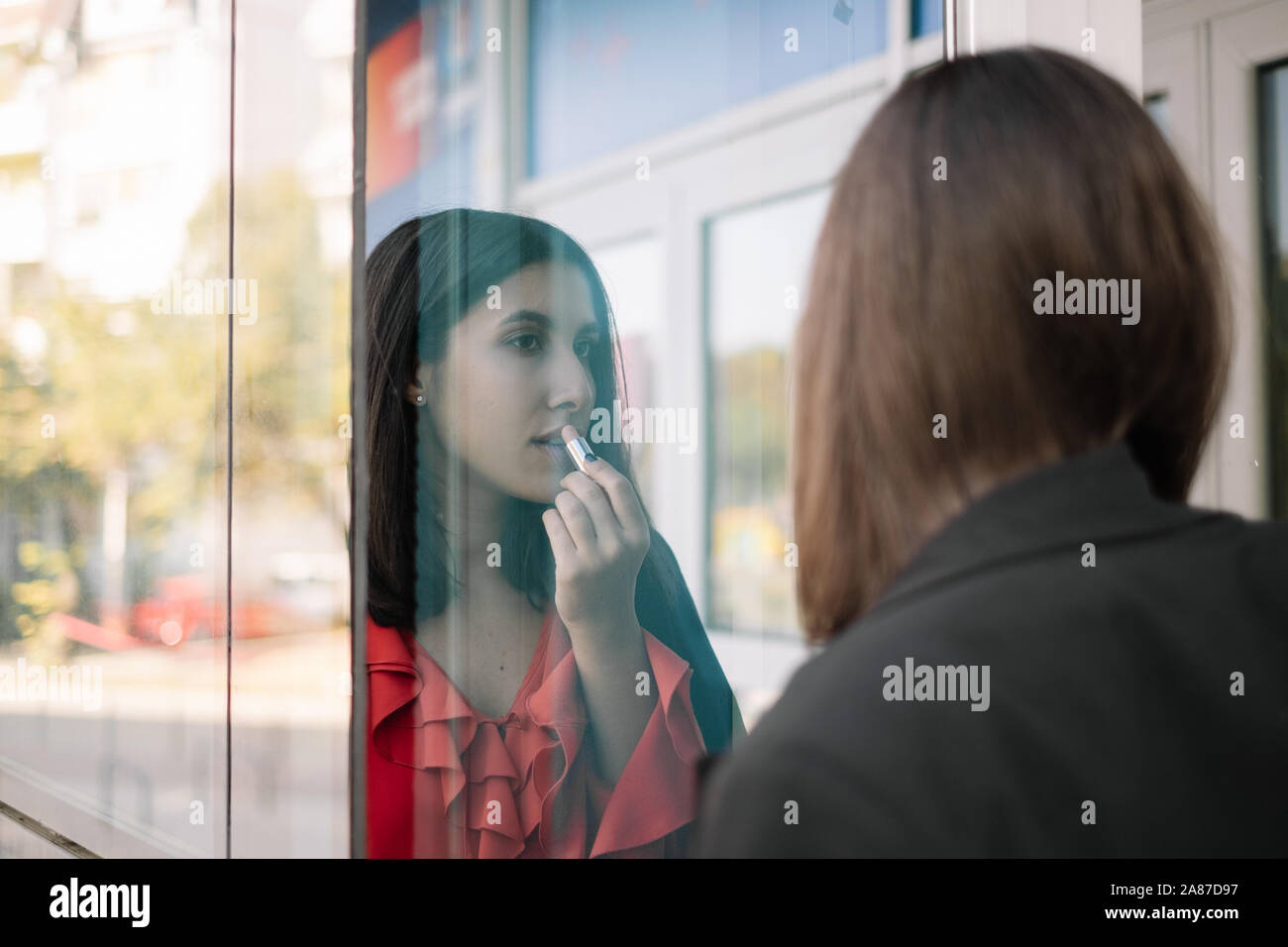 Woman applying lipstick while looking building glass wall Stock Photo ...