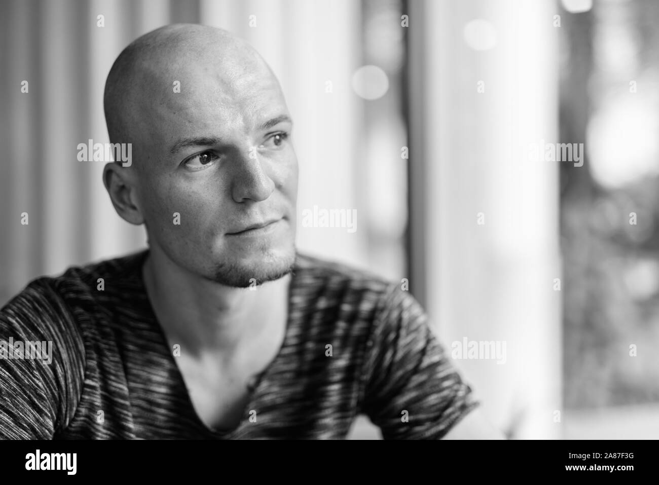 Face of young handsome bald man thinking inside restaurant with glass ...