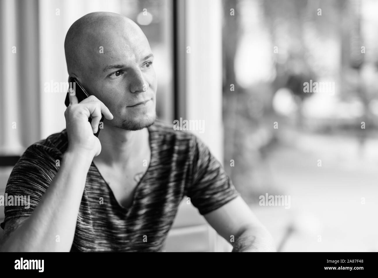 Young handsome bald man thinking while talking on mobile phone inside ...