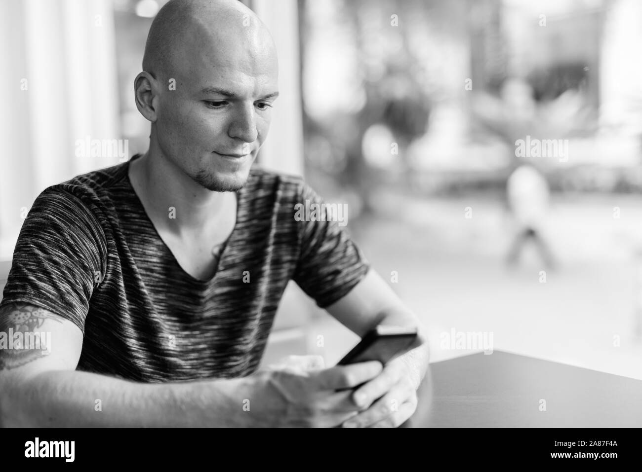 Young handsome bald man using mobile phone inside restaurant with glass ...