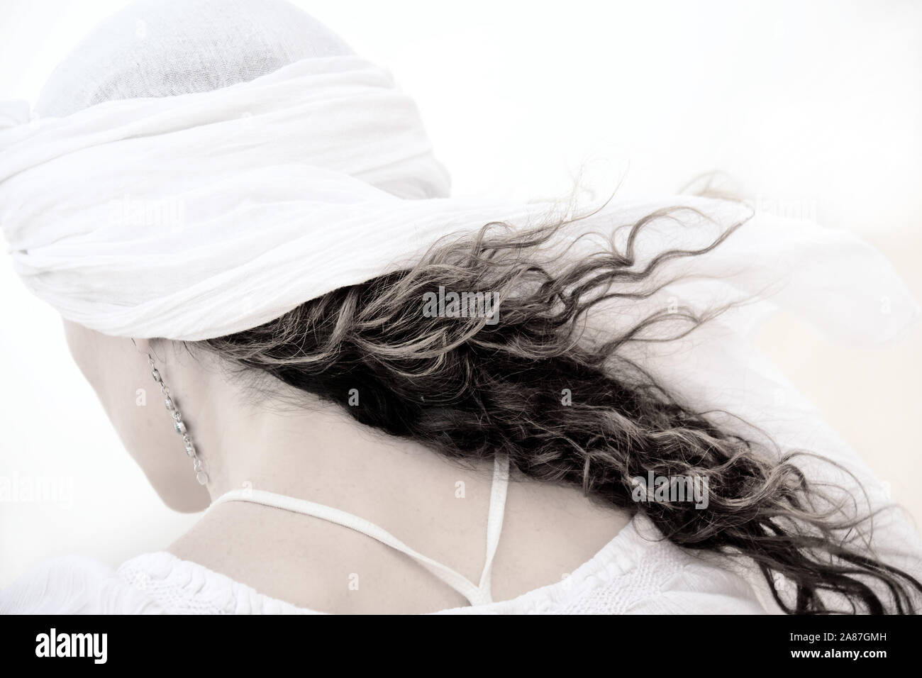 Woman with headscarf and curly long hair from behind. High key image ...