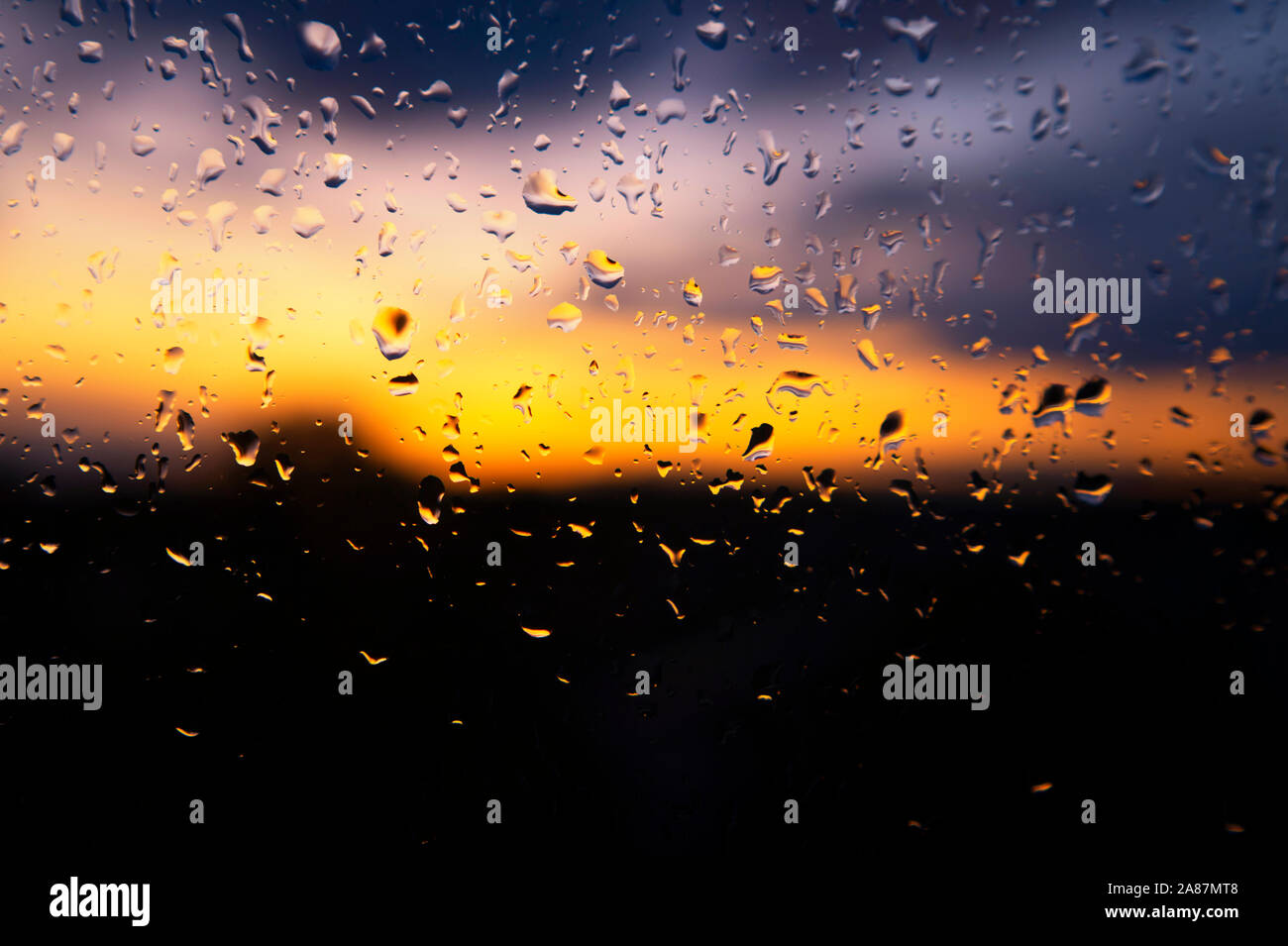 Colorful sunset through wet window glass with beaded raindrops and rivulets of water on a stormy ...