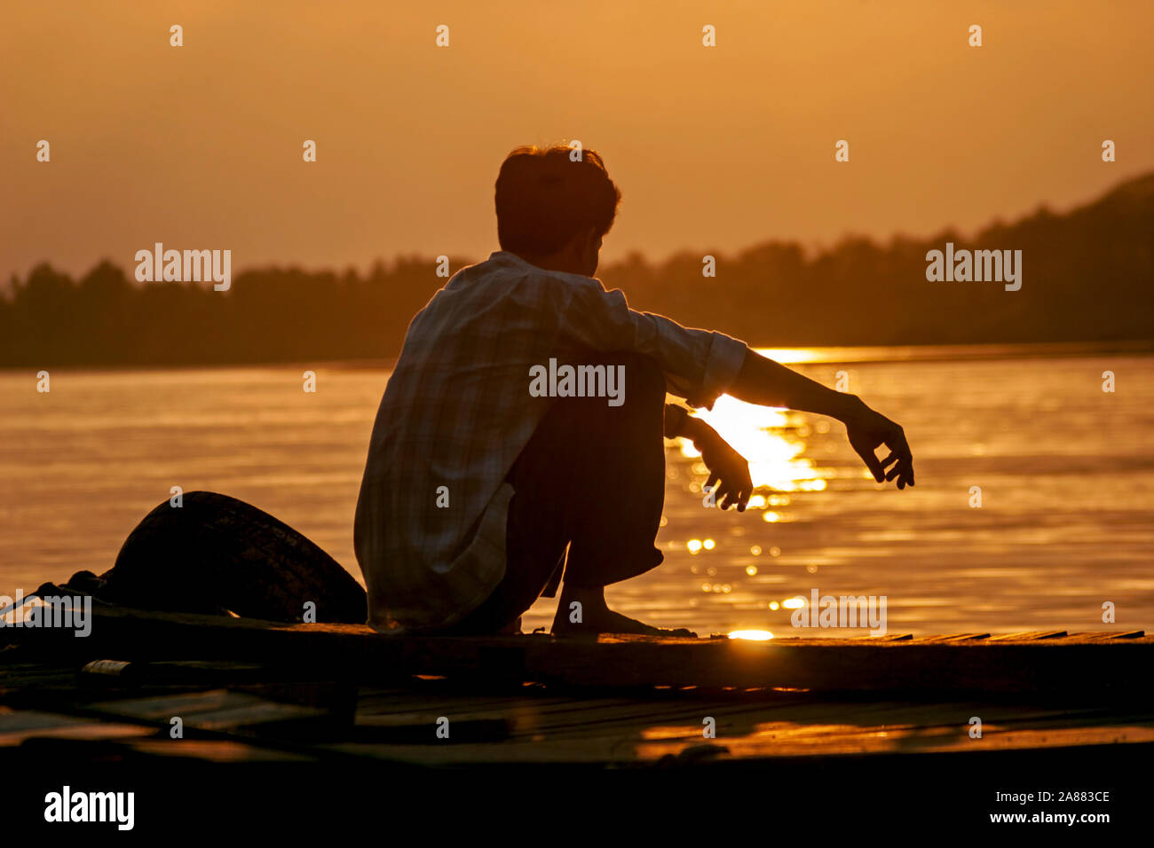 An Asian man is waiting for the sunset while relaxing on a wooden pier ...