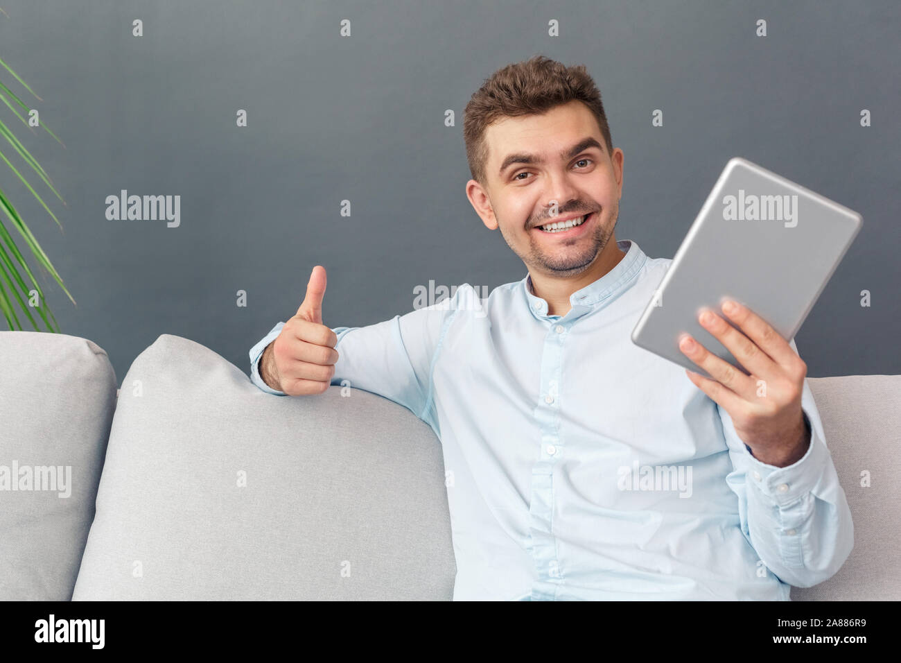 Freestyle. Young man studio sitting on sofa isolated on grey with ...