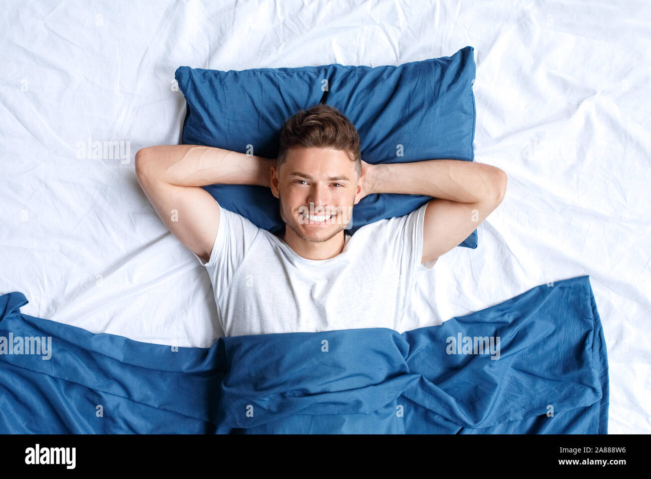 Bedtime. Guy lying on bed top view hands under head smiling relaxed ...
