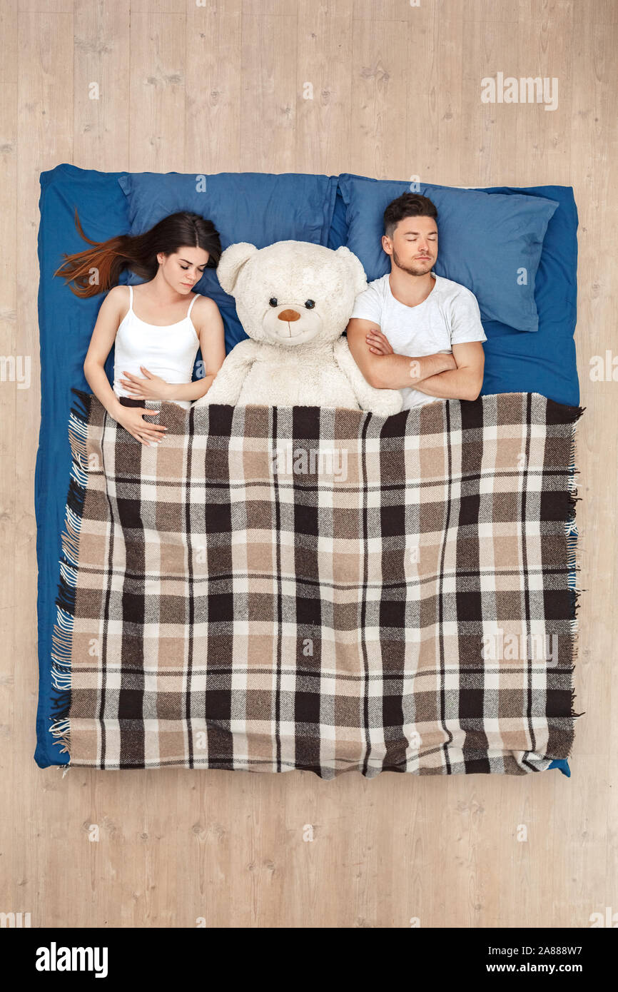 Bedtime. Young couple sleeping on bed top view under blanket with teddy ...