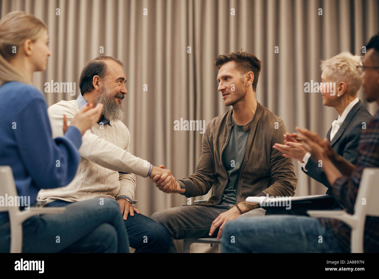 Two men sitting and shaking hands to each other while other people ...