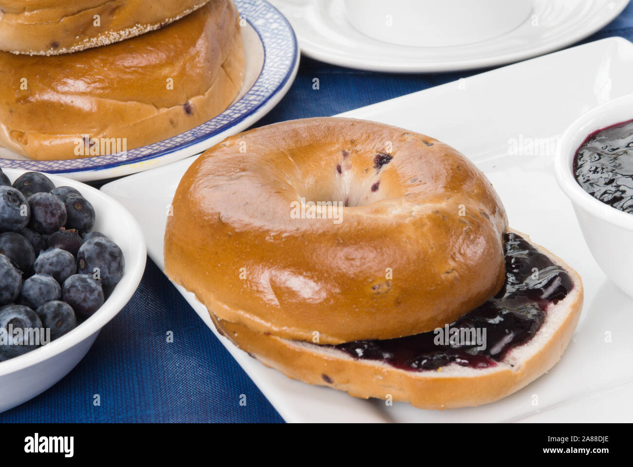 One sliced blueberry bagel filled with blueberry jam. There are side ...