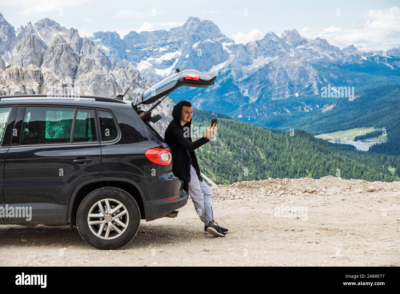 Young man sitting in the trunk of the car and use mobile phone on the ...