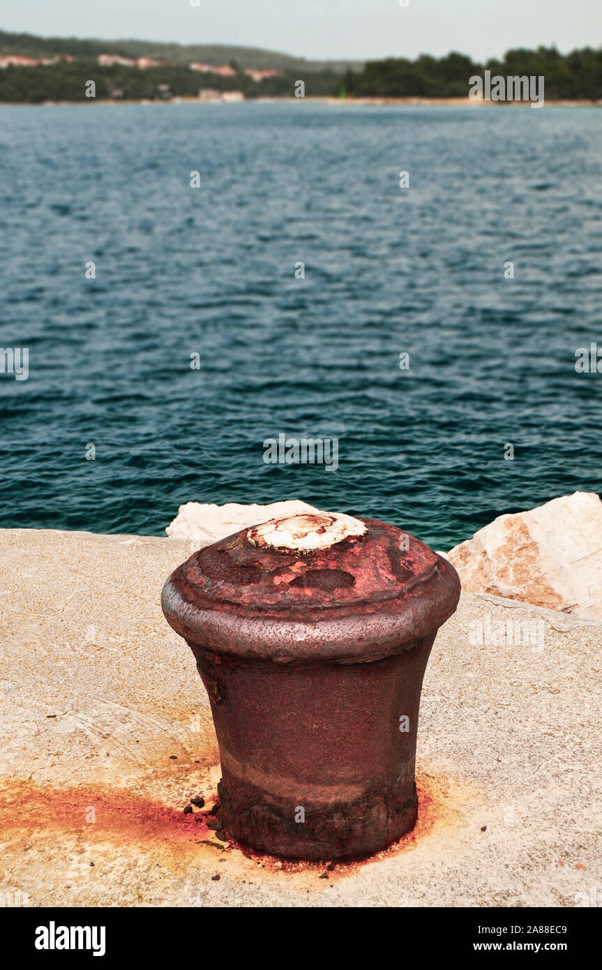 Old and rusty mooring post on concrete bank of port or harbour and blue ...