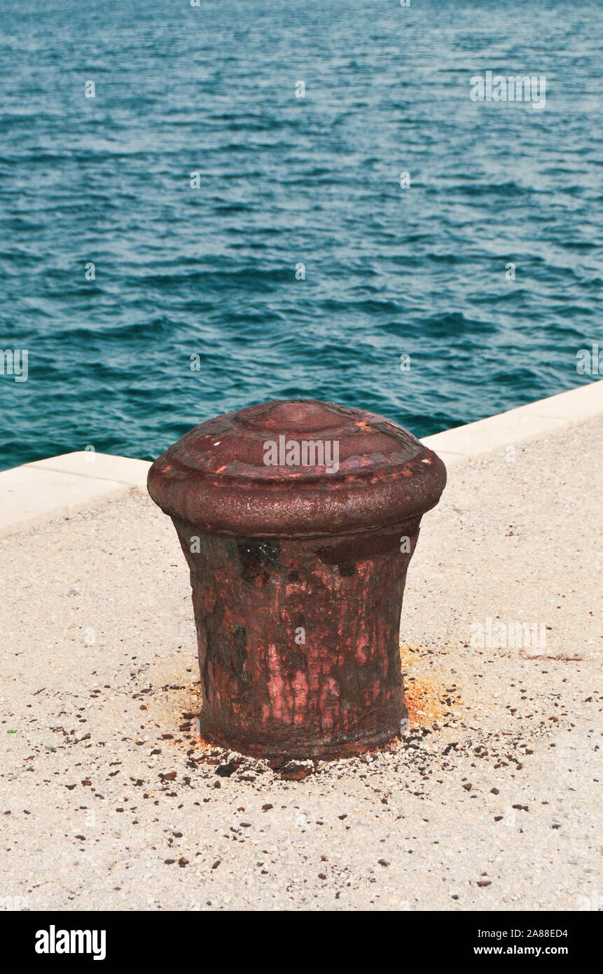 Old and rusty mooring post on concrete bank of port or harbour and blue ...
