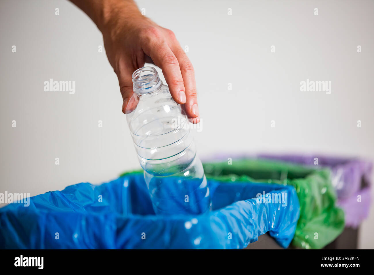 Hand putting single-use plastic bottle into recycling bin. Person in a ...