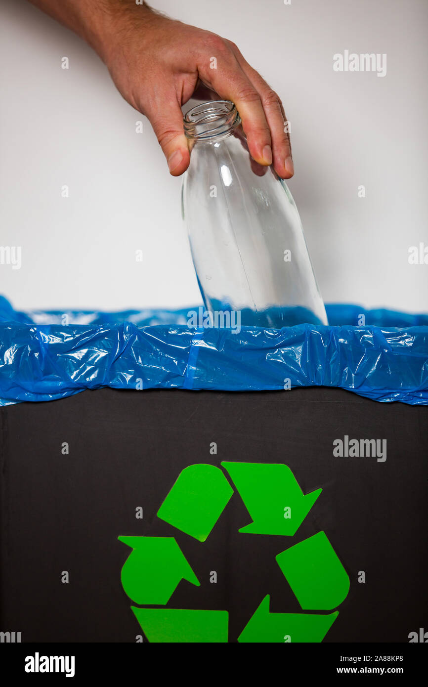Hand putting glass bottle into recycling bin. Person in a house kitchen separating waste. Black ...