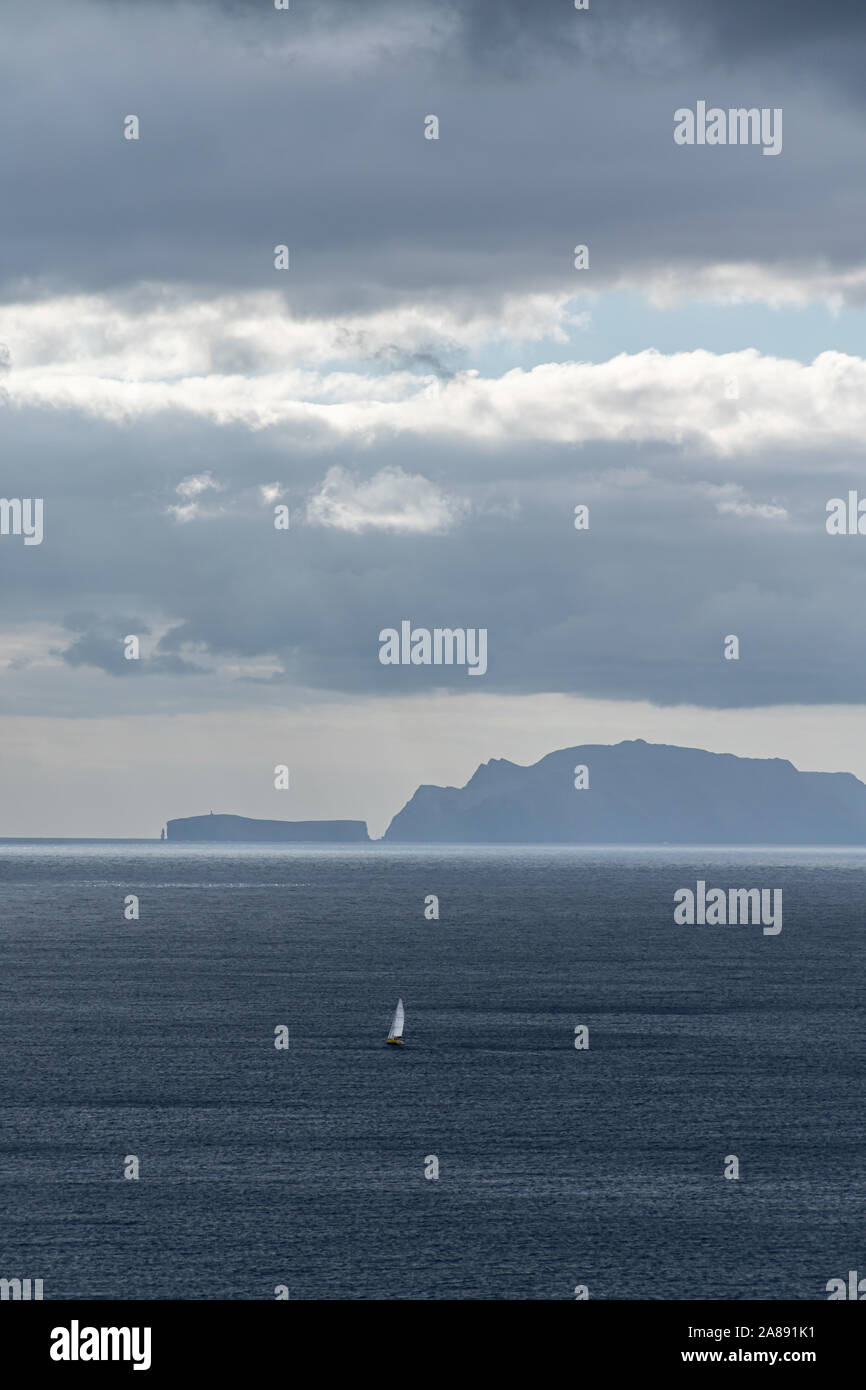 A small yacht sailing towards a distant island, sunbeams passing ...